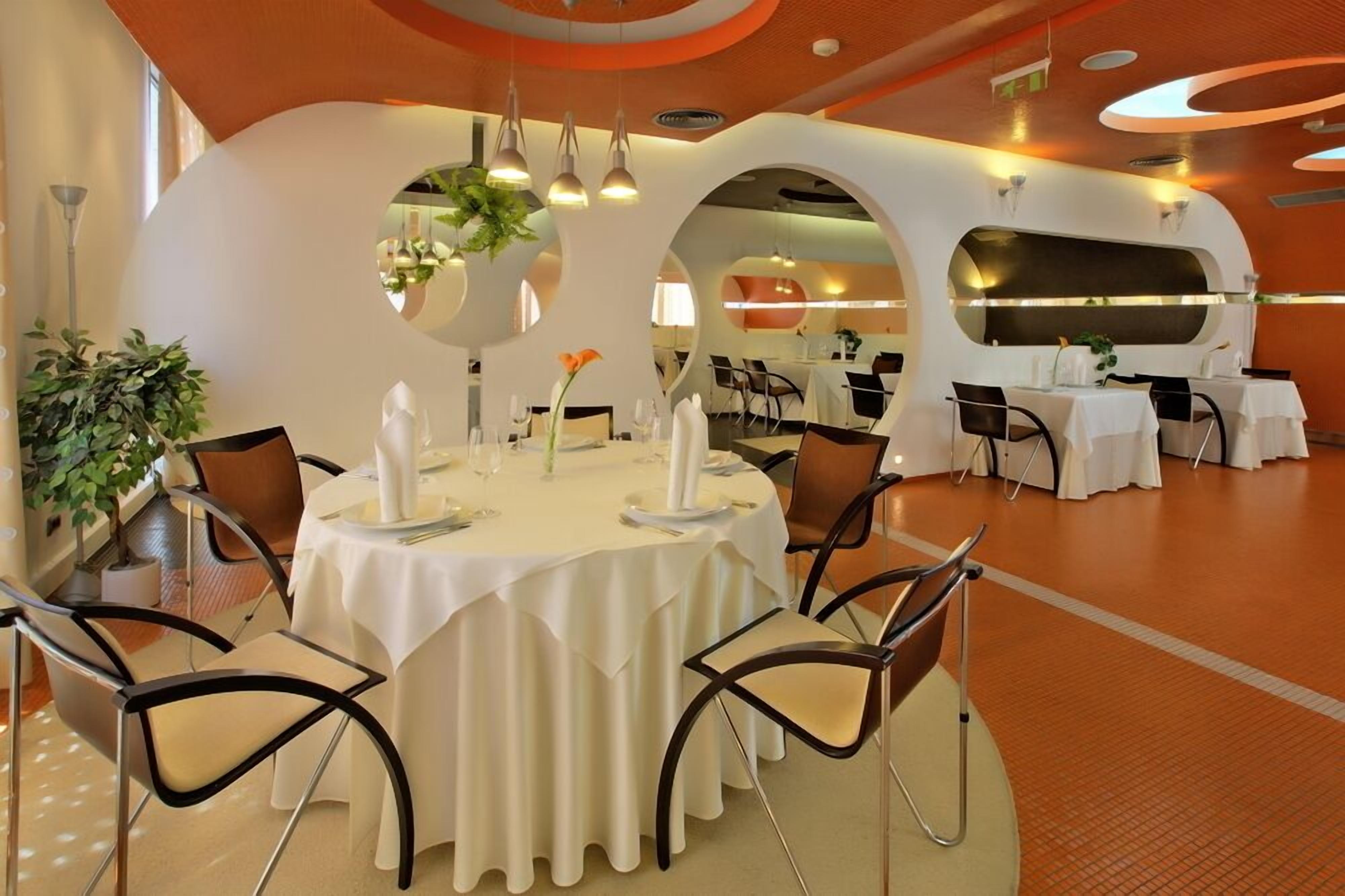 Restaurante com mesas redondas, toalhas brancas e cadeiras modernas.