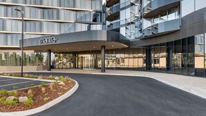 Um edifício moderno com entrada curva, um letreiro com a palavra 'mantra' e um estacionamento com área ajardinada.