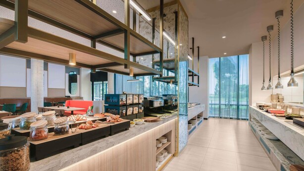 Uma área de jantar de hotel moderna com um balcão extenso, diversos alimentos e vista para o exterior.