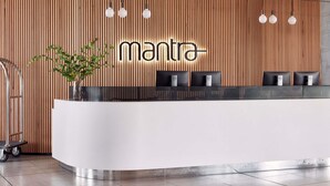 Uma receção com parede de ripas de madeira, uma planta e um sinal com a palavra 'mantra'.