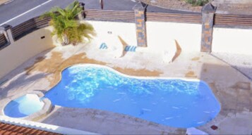 Piscina com um pequeno ofurô, rodeada por um deck de concreto e um muro de pedra baixo.