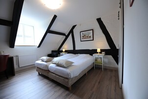 Quarto com uma cama grande, duas mesas de cabeceira, um criado-mudo, radiador, janela e um quadro na parede.