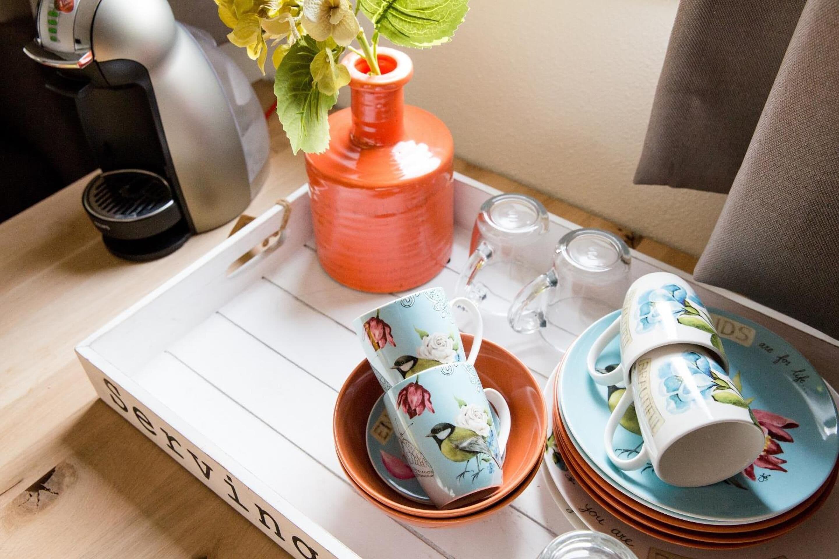 Uma bandeja com uma cafeteira, um vaso com flores, uma caneca e um prato com um desenho floral.