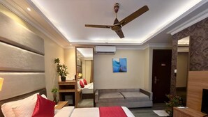 Quarto de hotel com cama, sofá, televisão e ventoinha no teto.