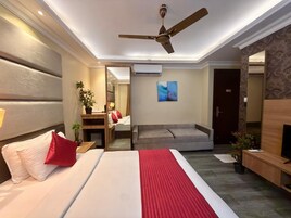 Quarto de hotel com cama, sofá, televisão e ventoinha no teto.