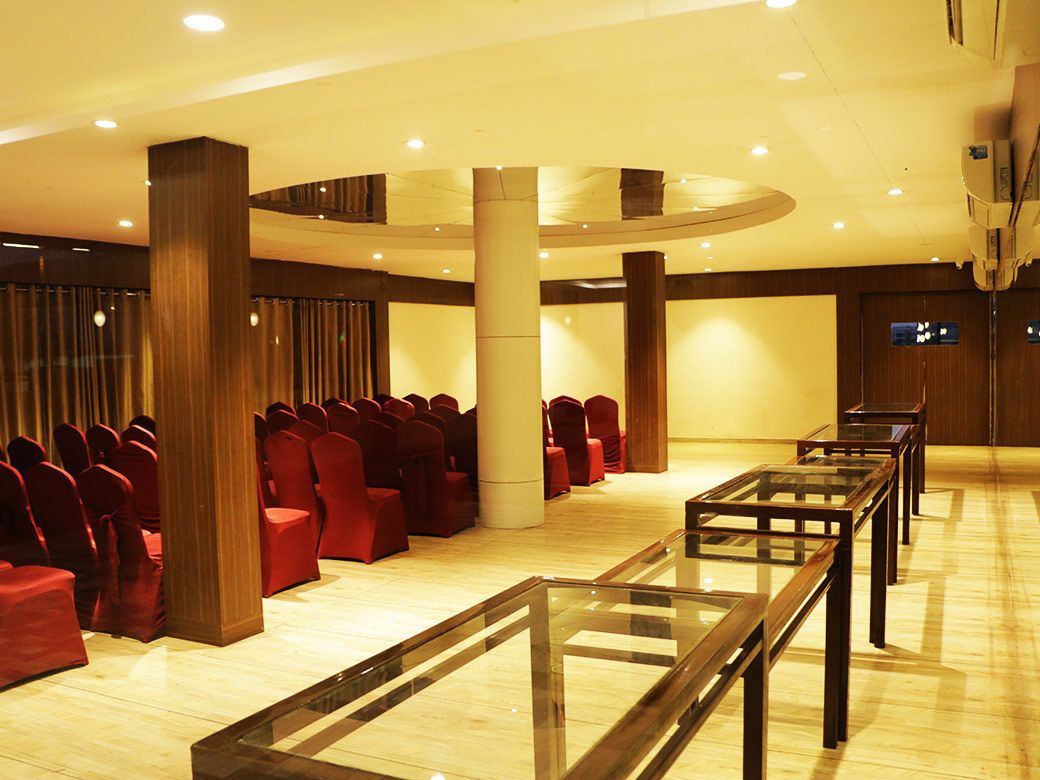 Uma sala de conferências com fileiras de cadeiras vermelhas, uma mesa de vidro e piso de madeira.