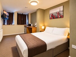 Quarto de hotel com cama, escrivaninha, cadeira, televisão e pintura da Torre Eiffel.