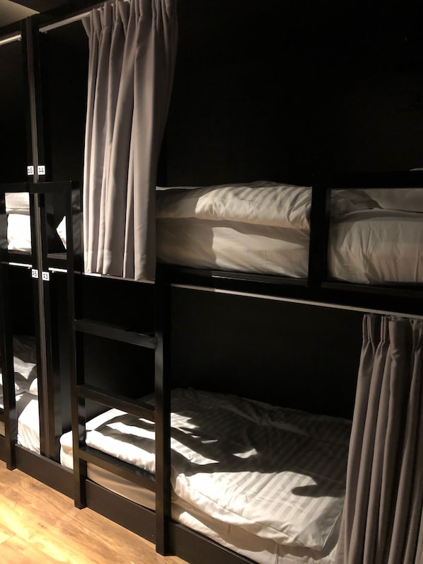 Quarto com beliches, cortinas, piso de madeira e camas numeradas.