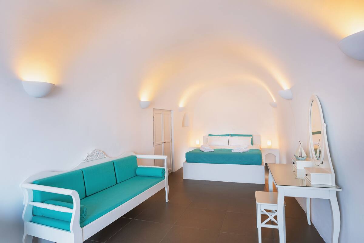 Quarto de hotel moderno com uma cama, uma escrivaninha branca, uma cadeira branca e um sofá verde-água.