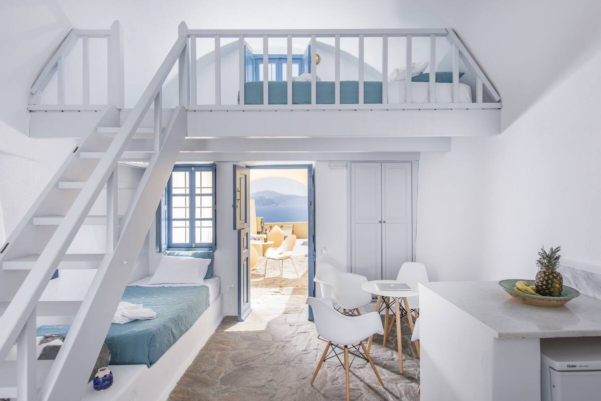 Quarto compacto e moderno com beliche, área de refeições com mesa e cadeiras, e vista para o exterior.