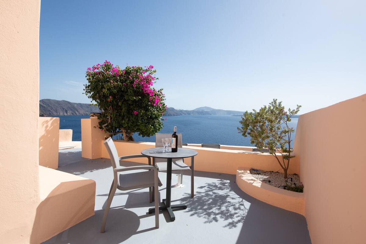 Terraço com mesa e cadeiras, uma garrafa de vinho e vista para o mar.