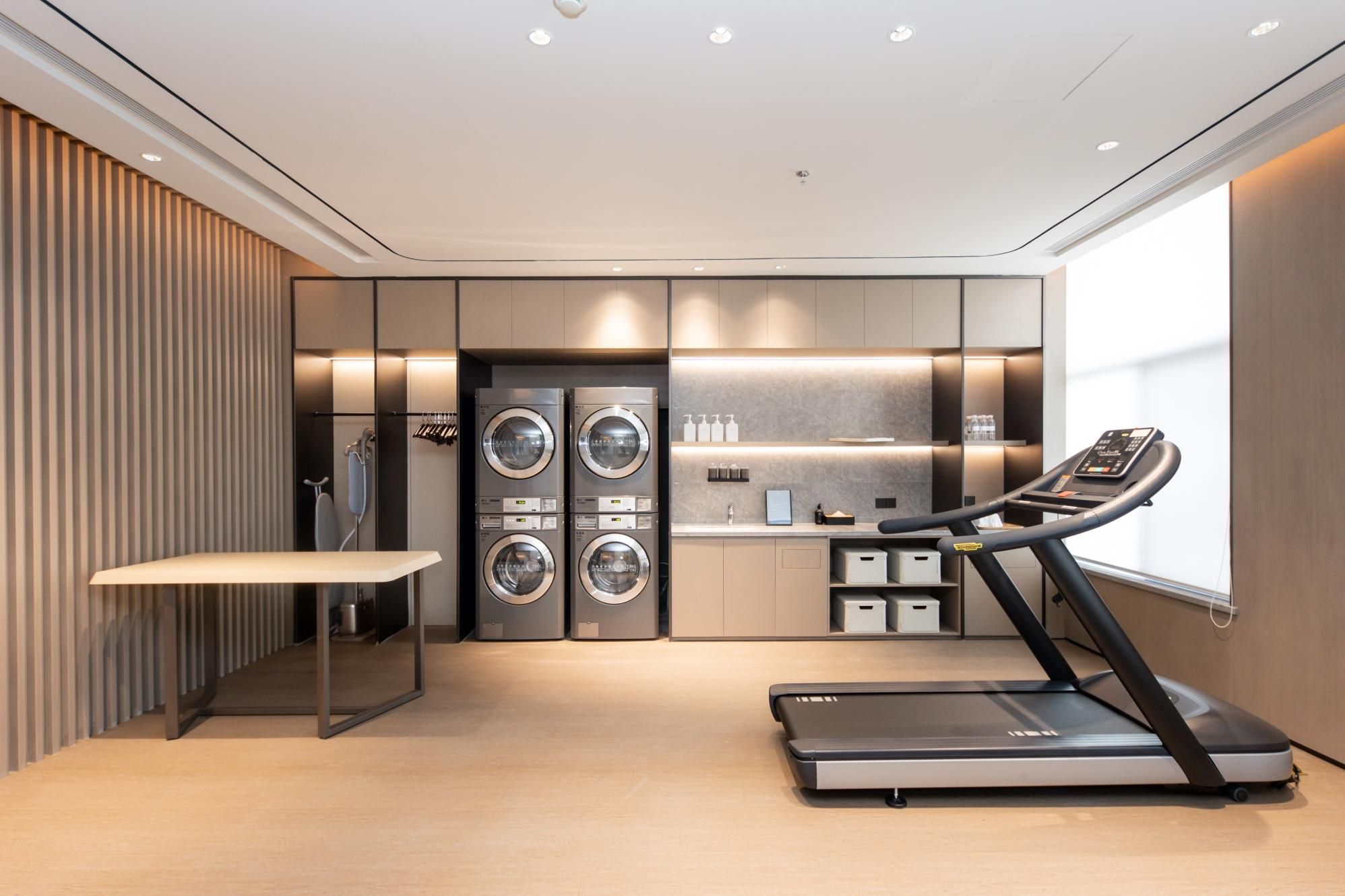 Quarto de hotel moderno com esteira ergométrica, máquinas de lavar roupa e uma toucador com espelho.
