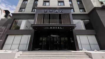 Entrada de um hotel moderno com um letreiro destacado, um conjunto de degraus que levam à entrada e fachada de vidro.