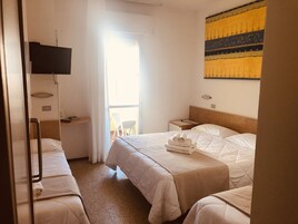Quarto de hotel com duas camas, televisão na parede, mesa com cadeira e janela com cortinas.