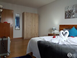 Quarto de hotel com cama, guarda-roupa de madeira, espelho, radiador e um quadro na parede.