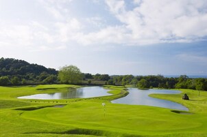 Um campo de golfe com vários lagos e uma bandeira ao primeiro plano.