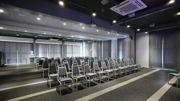 Uma sala de conferências com fileiras de cadeiras, um projetor e uma janela grande.