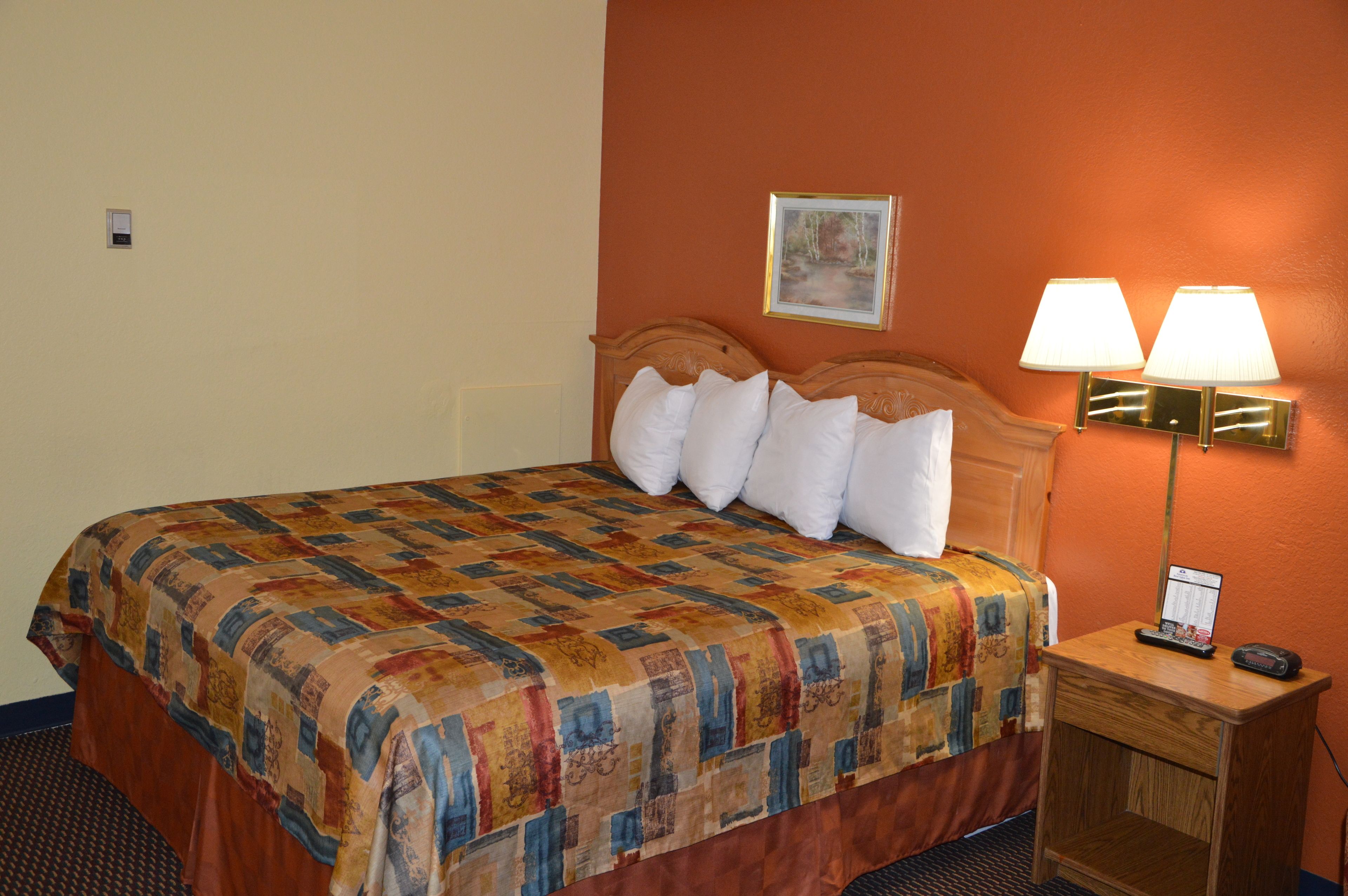 Quarto de hotel com uma cama, mesa de cabeceira com abajur e um quadro na parede.