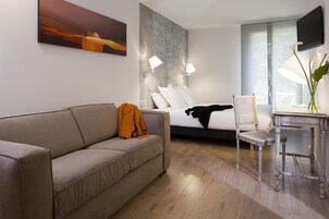 Quarto de hotel moderno com sofá, cama, escrivaninha com cadeira, televisão e um quadro na parede.