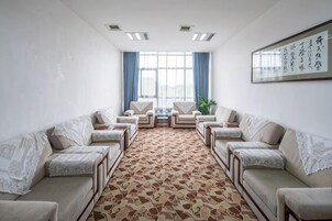 Uma sala de conferências com carpete estampado, dois sofás um de frente para o outro, uma mesa e uma janela com cortinas.