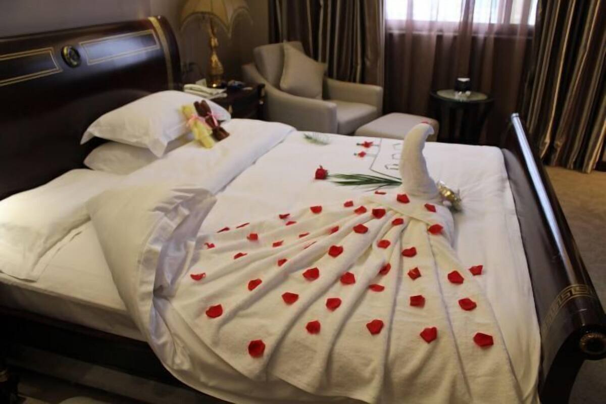 Cama bem arrumada com lençóis brancos e pétalas de rosa vermelha dispostas em formato de leque.