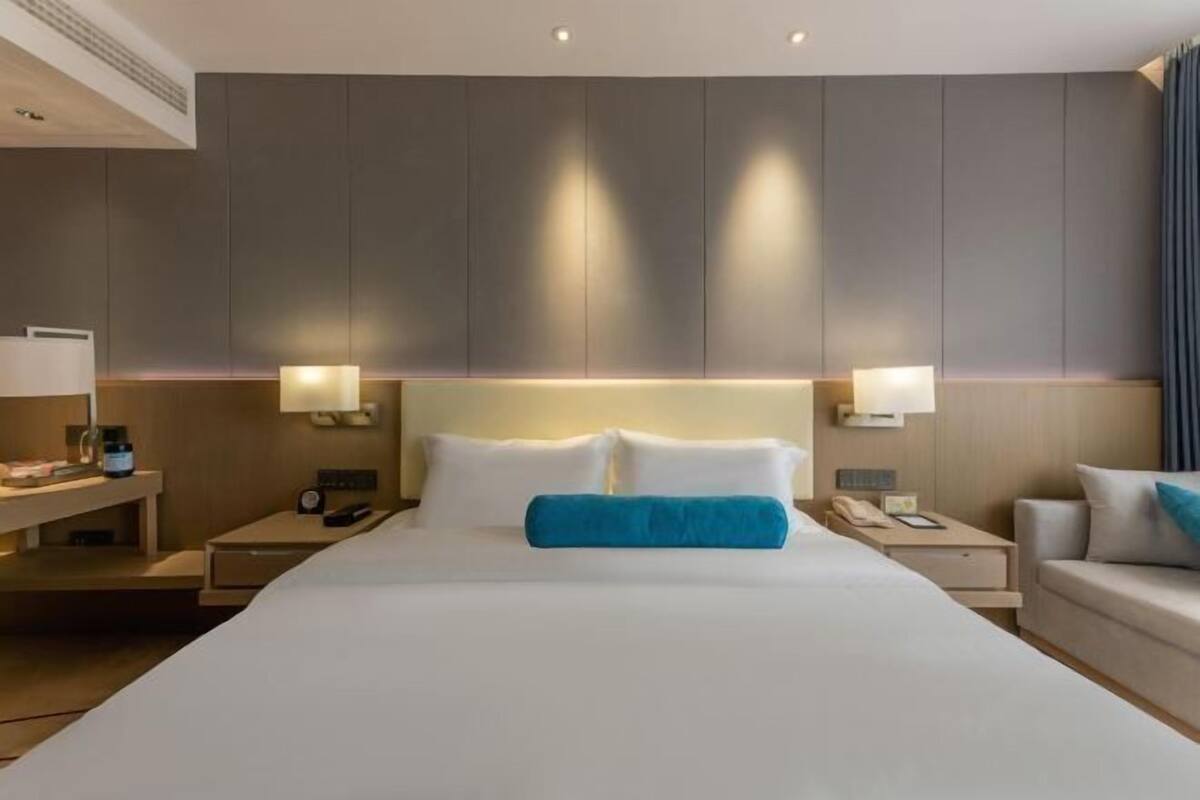 Quarto de hotel com cama grande, mesas de cabeceira, um abajur e um sofá.