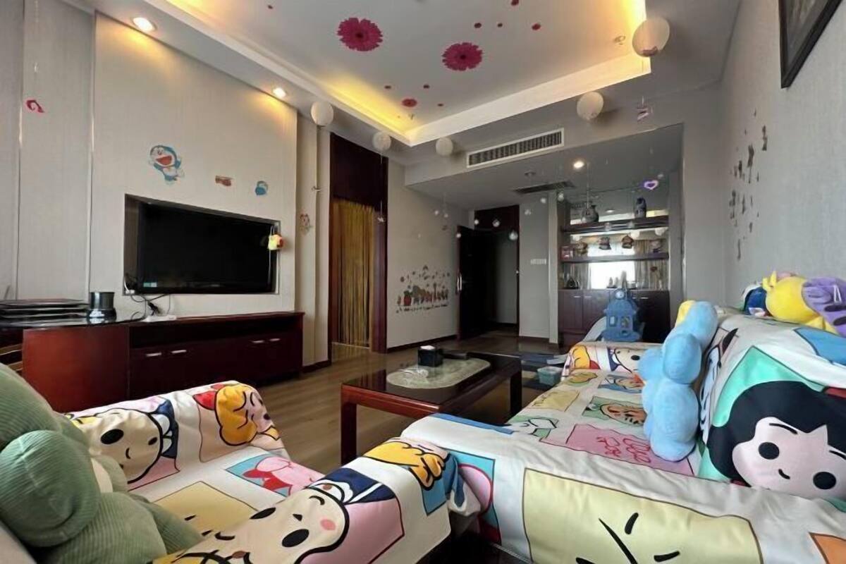 Uma sala de estar com televisão, um sofá com estampas de desenhos animados, uma mesa de centro e uma cama com colcha temática de cartoons.