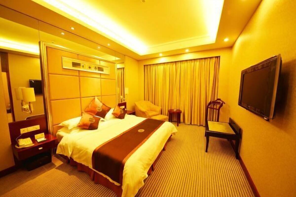Quarto de hotel com uma cama grande, mesas de cabeceira, televisão e janela com cortinas.