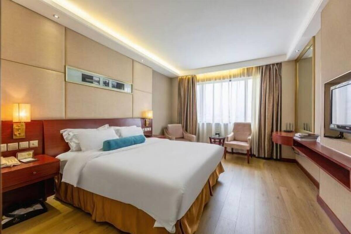 Quarto de hotel com uma cama grande, mesas de cabeceira, televisão e uma janela com cortinas.