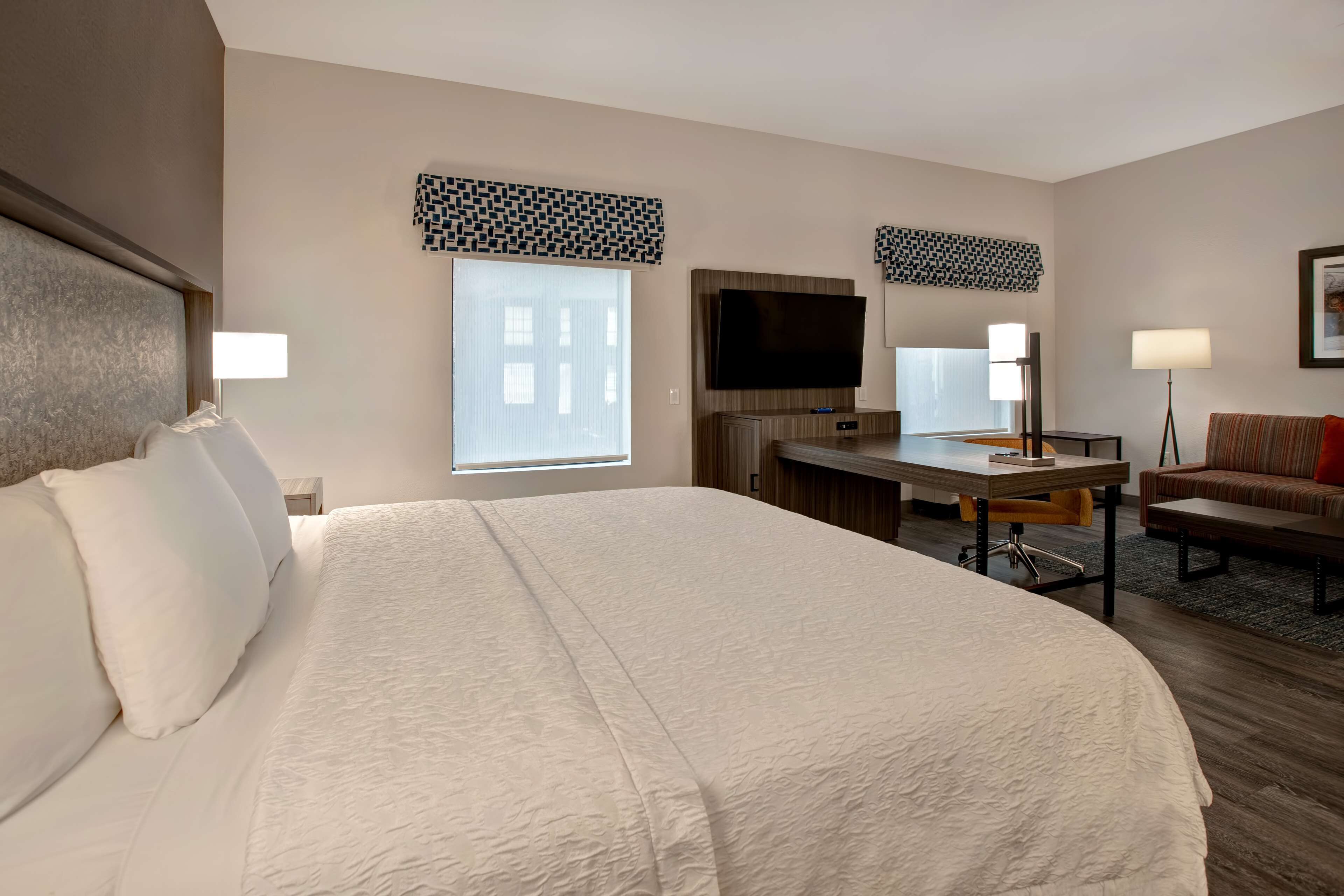 Quarto de hotel com uma cama grande, uma escrivaninha, uma televisão e um sofá.