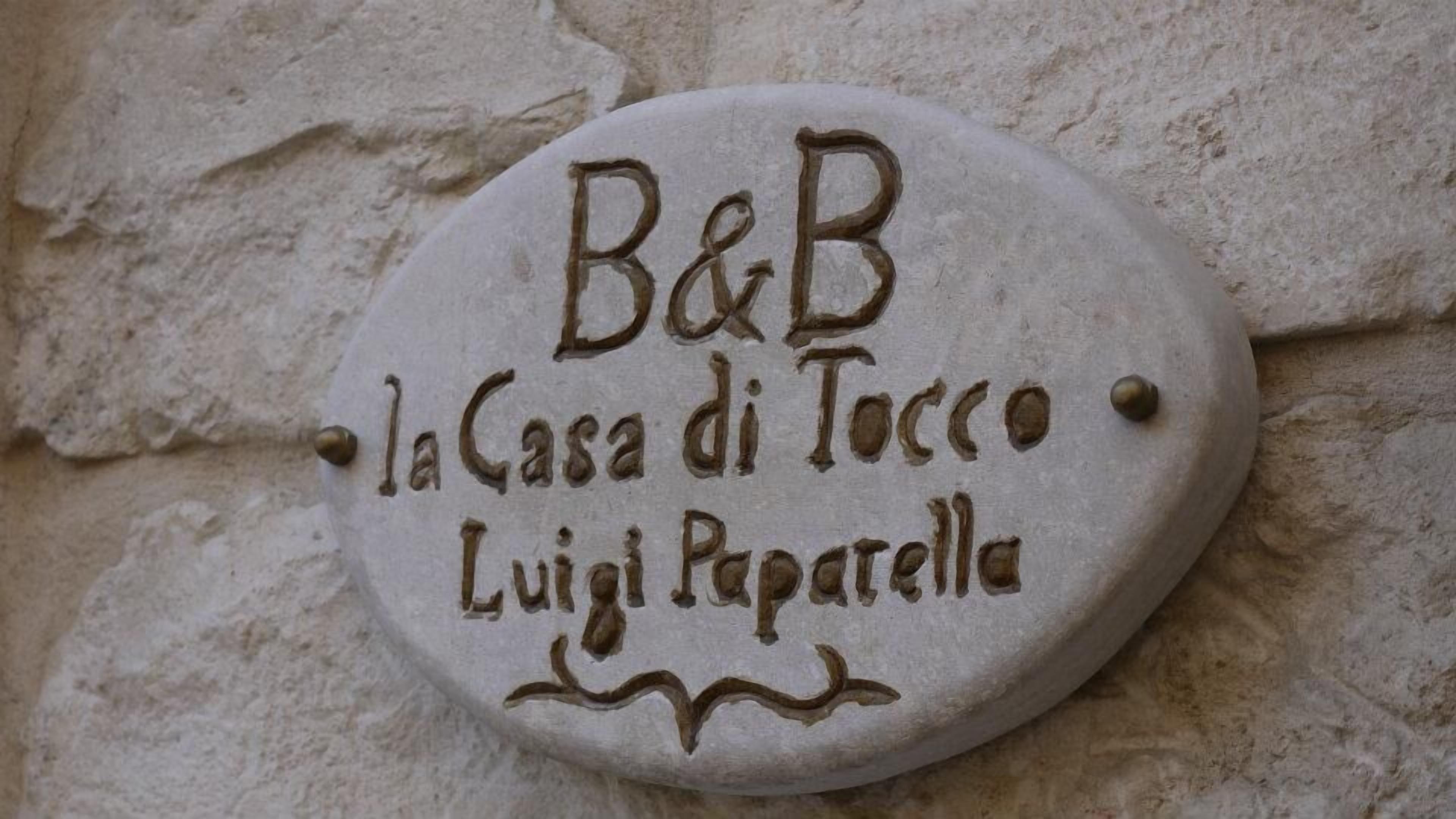 Placa de pedra com a inscrição "B&B laCasa di Tocco Luigi Paparella" fixada numa parede com textura.
