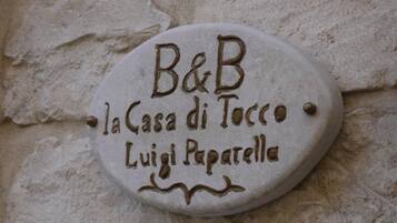 Placa de pedra com a inscrição "B&B laCasa di Tocco Luigi Paparella" fixada numa parede com textura.