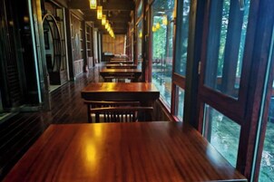 Fileira de mesas e bancos de madeira em um restaurante com janelas amplas.