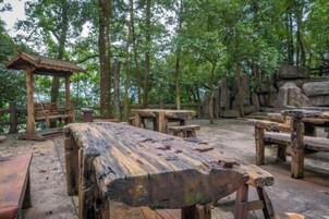 Um deck de madeira ao ar livre com bancos e mesas, rodeado por árvores.