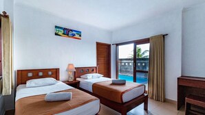 Quarto de hotel com duas camas, uma escrivaninha, uma luminária e vista para uma piscina.