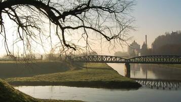 Uma ponte sobre um rio calmo, com uma árvore em primeiro plano e um edifício ao fundo.