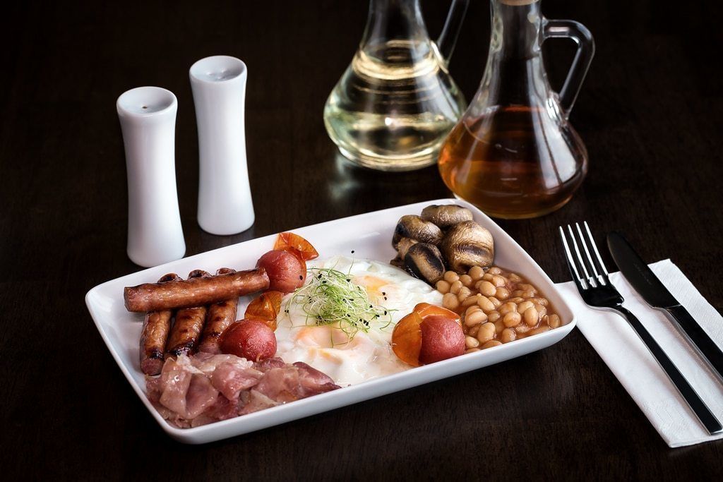 Prato de café da manhã com linguiça, ovos, cogumelos e feijão.