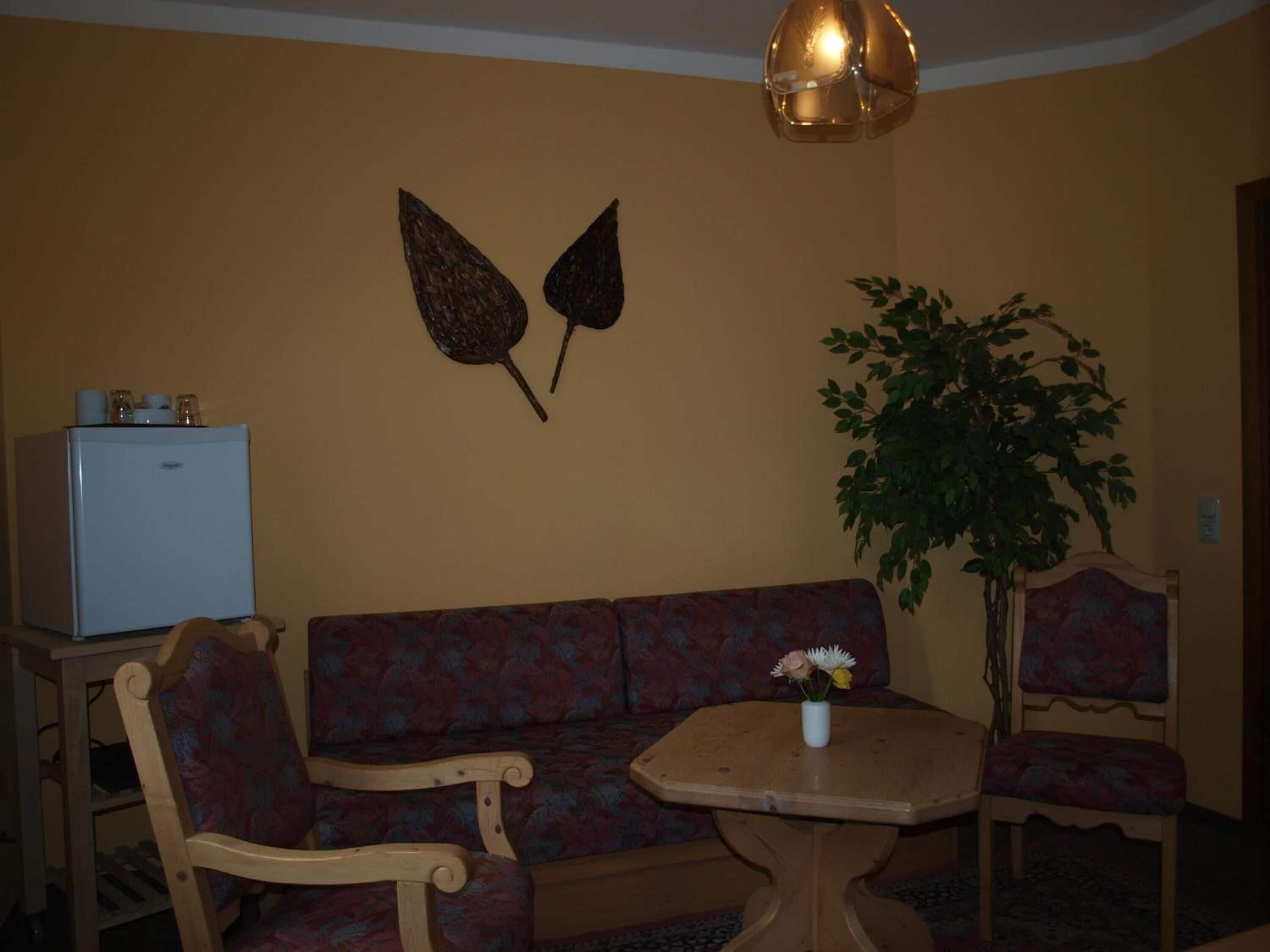 Sala de estar com sofá, duas poltronas, mesa pequena, planta e luminária na parede.