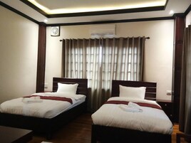 Quarto de hotel com duas camas, ventoinha no teto e janela com cortinas.