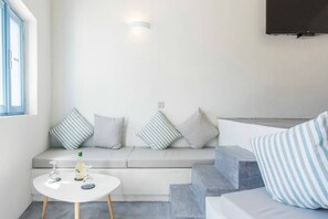 Uma sala de estar moderna com um sofá cinzento, almofadas listradas, uma mesa de centro branca e uma televisão na parede.