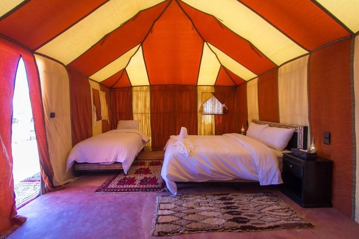 Um quarto com tenda, duas camas, uma mesa de cabeceira e um abajur.