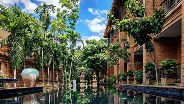Um pátio de hotel tranquilo com uma piscina espelhada, vegetação exuberante e arquitetura tradicional.