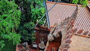 Uma estrutura arquitetônica tradicional tailandesa com esculturas detalhadas, telhado com telhas e uma pequena área externa com mesa e cadeiras.