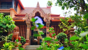 Um edifício tradicional com entrada imponente, escadaria que o leva e vegetação ao redor.