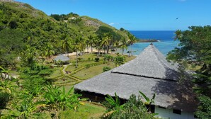 Uma casa com telhado de palha e vista para o oceano e vegetação exuberante.