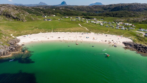Vista aérea de uma área costeira com praia de areia, marina e um conjunto de casas.