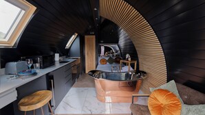Cozinha compacta e moderna com uma pia grande de cobre, um banquinho de madeira e uma área de refeições com mesa e cadeiras.