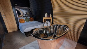 Um banheiro moderno com banheira livre, toucador de madeira, cama com travesseiros e mesa de cabeceira.