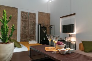 Quarto de hotel moderno com cama, mesa de jantar, vaso de flores, televisão e planta cacto.
