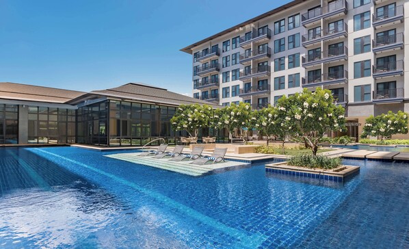 Um hotel moderno com uma grande piscina ao ar livre, quartos com paredes de vidro e um jardim bem cuidado.
